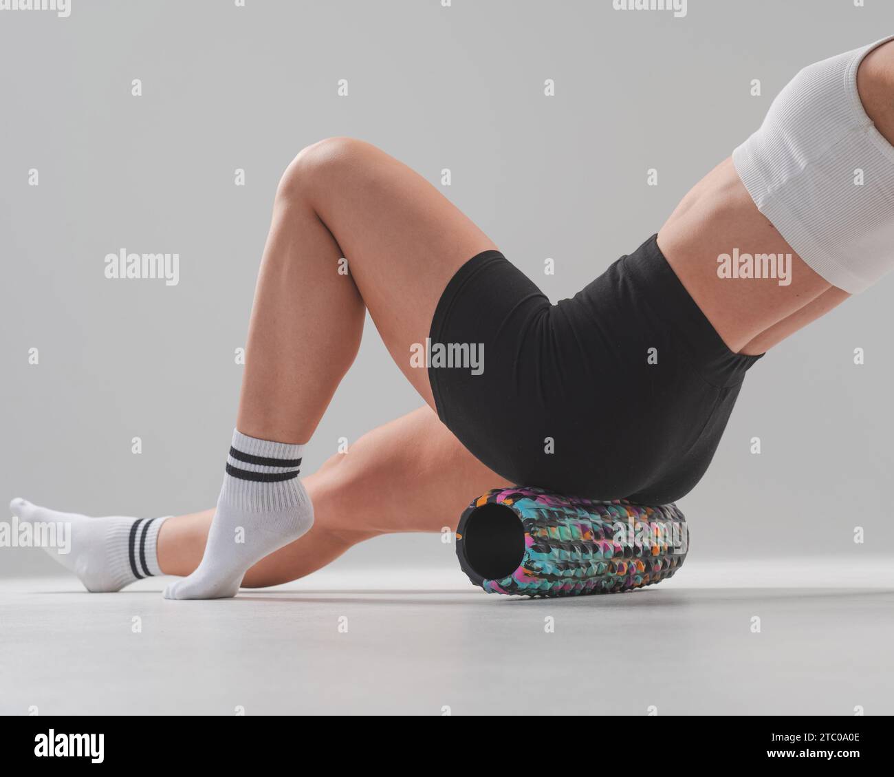 Faceless woman doing roller exercise for myofascial release on white ...