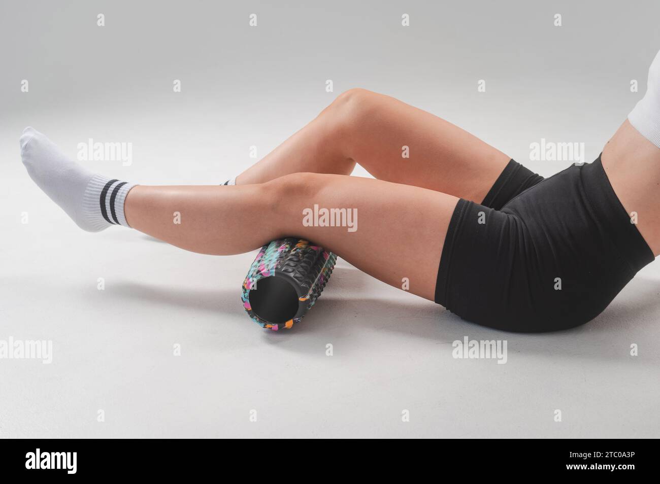 Faceless woman doing roller exercise for myofascial release on white ...