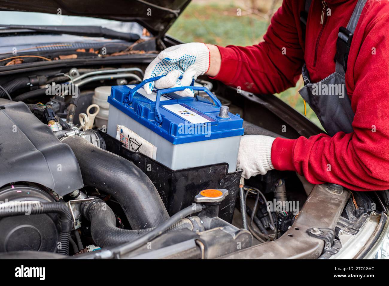 A man installs a car battery under the hood of a car. Vehicle ...