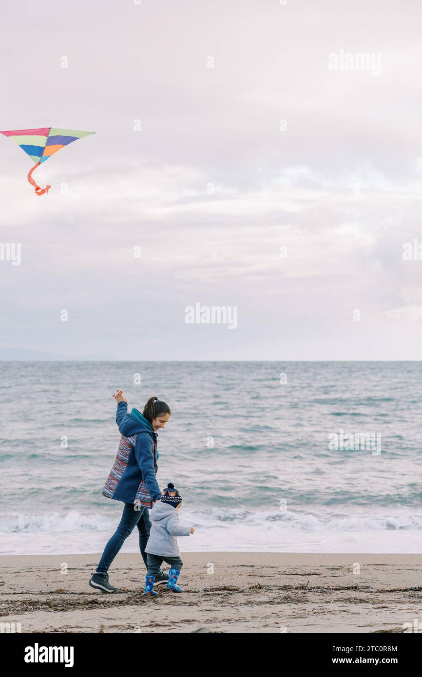 Mom with a kite on a string walks with a little girl by the hand along ...