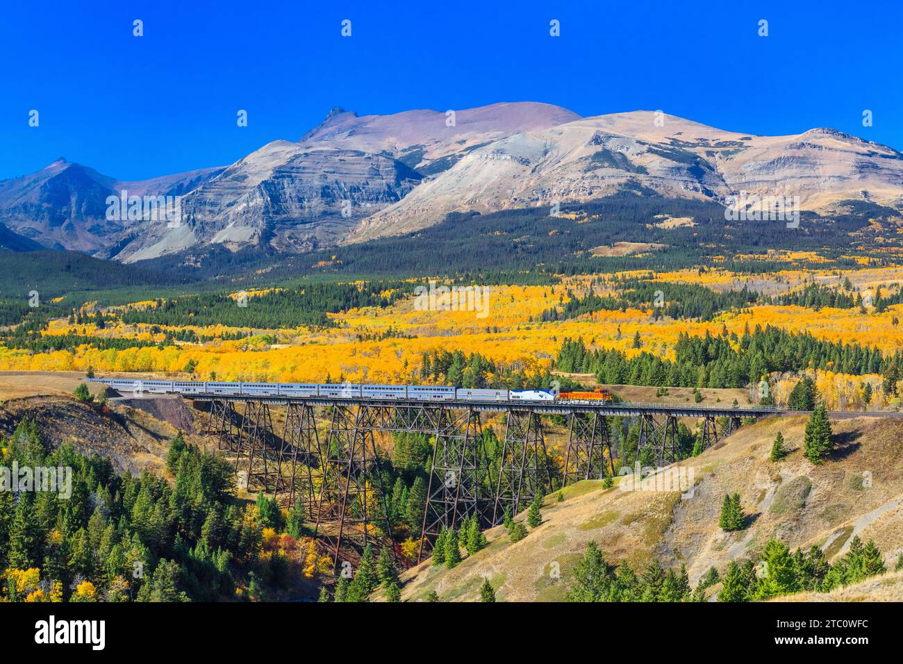 passenger train crossing over a trestle in autumn below peaks of ...