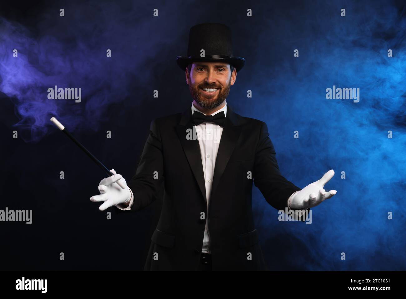Happy magician holding wand in smoke on dark background Stock Photo - Alamy