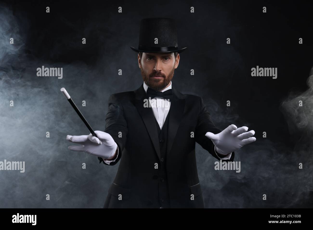 Magician holding wand in smoke on black background Stock Photo - Alamy