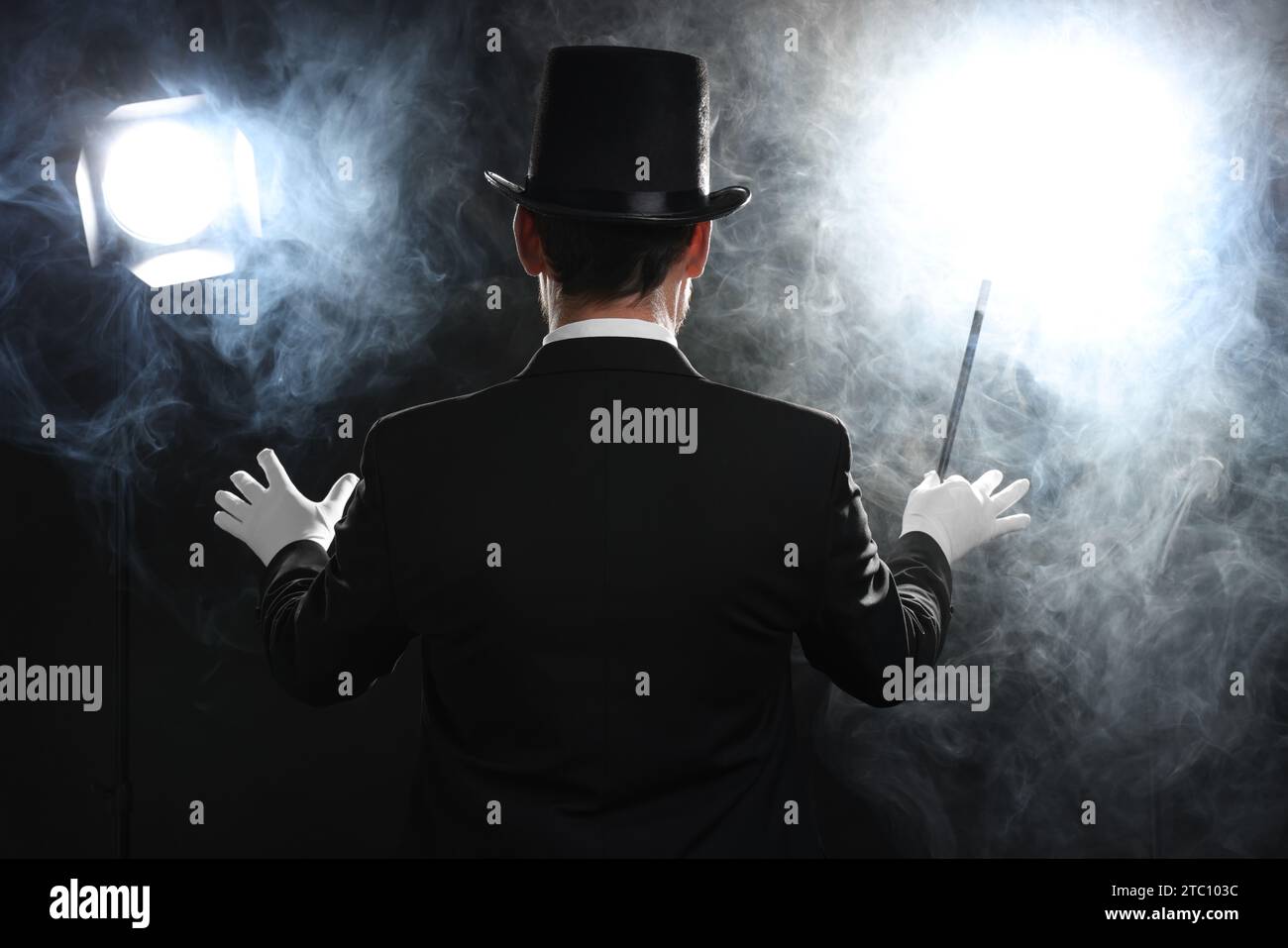 Magician with wand in smoke on stage, back view Stock Photo - Alamy