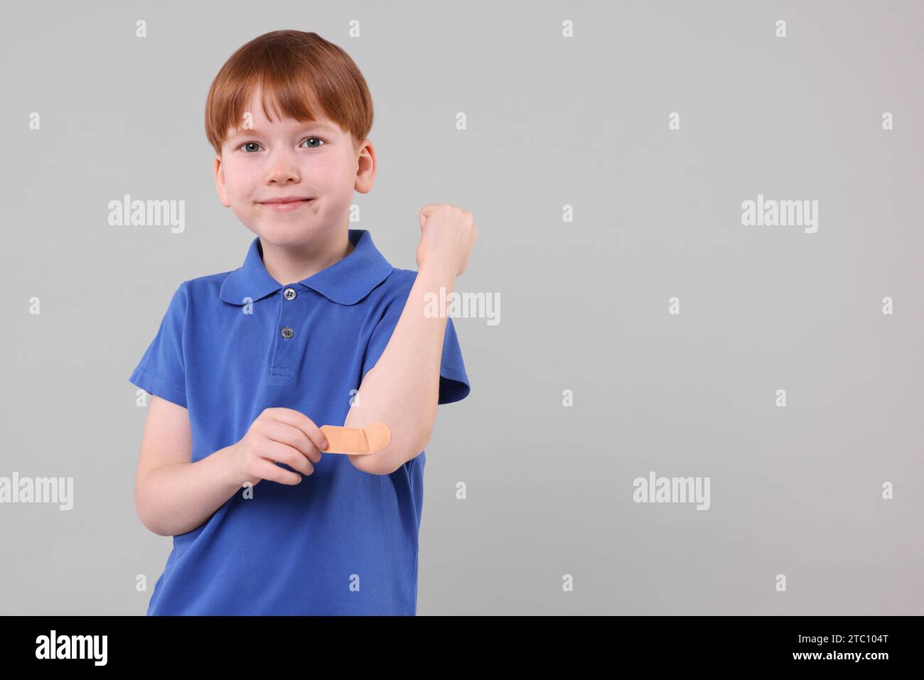 Little boy putting sticking plaster onto elbow against light grey ...