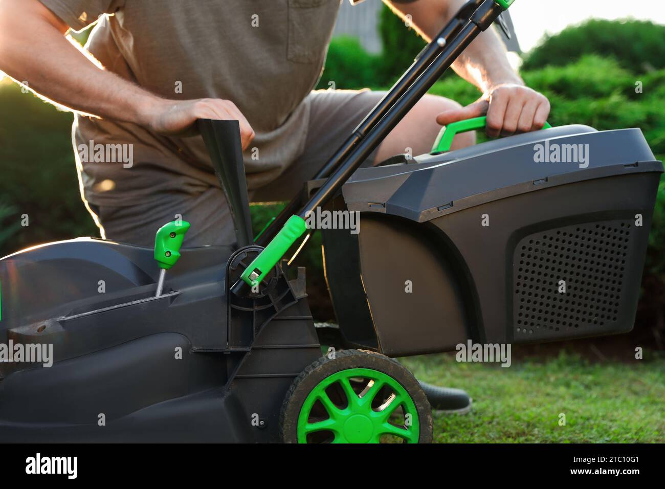 Cleaning lawn mower. Man detaching grass catcher from device in garden ...