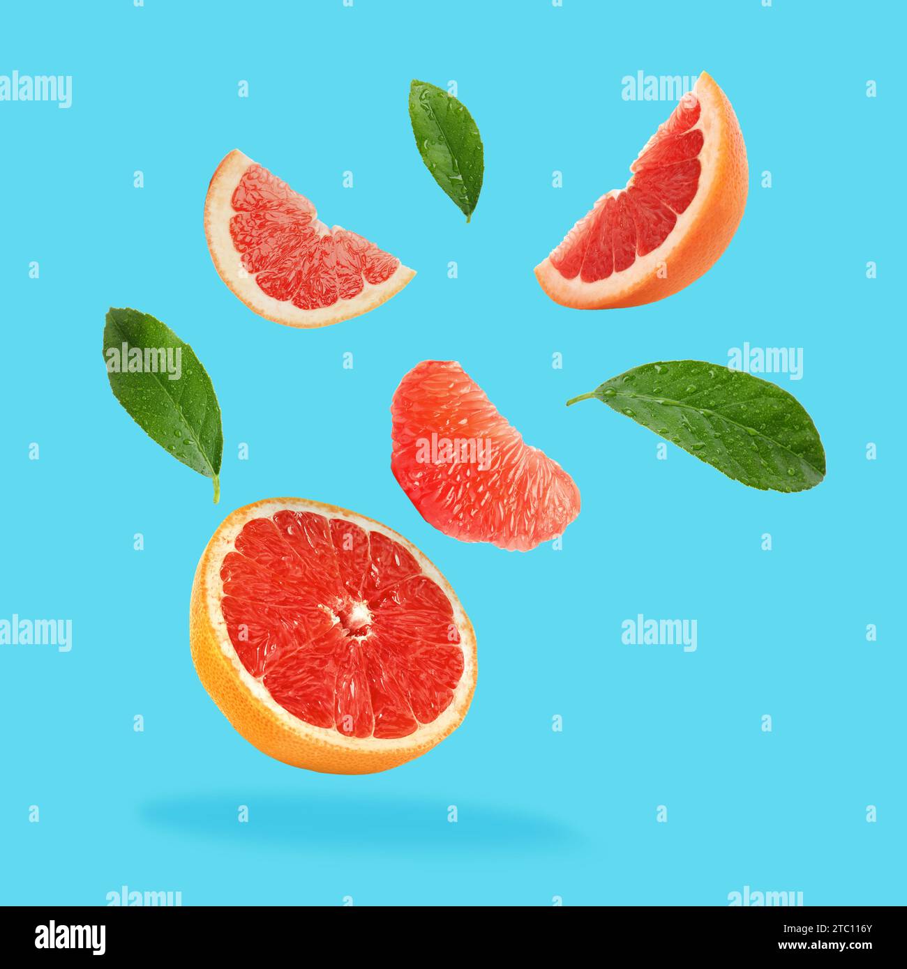 Pieces of grapefruit and green leaves falling on light blue background ...