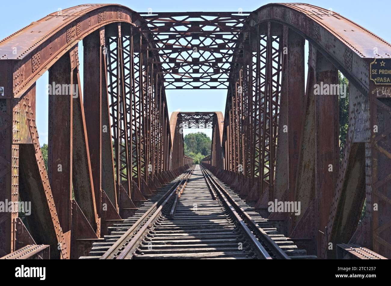 A rusty metal railroad bridge with tracks extending into the distance ...