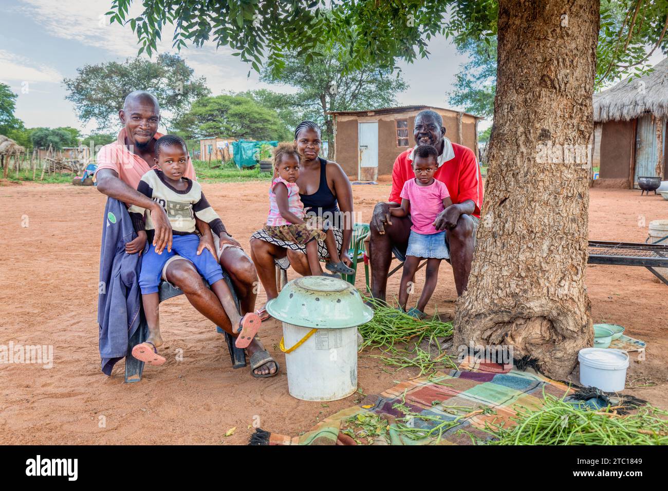 village african family, sited in the yard in front of the house, hut with thatched roof in the ...