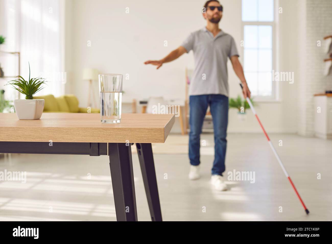 Blind man with stick is walking towards table with glass of water in ...