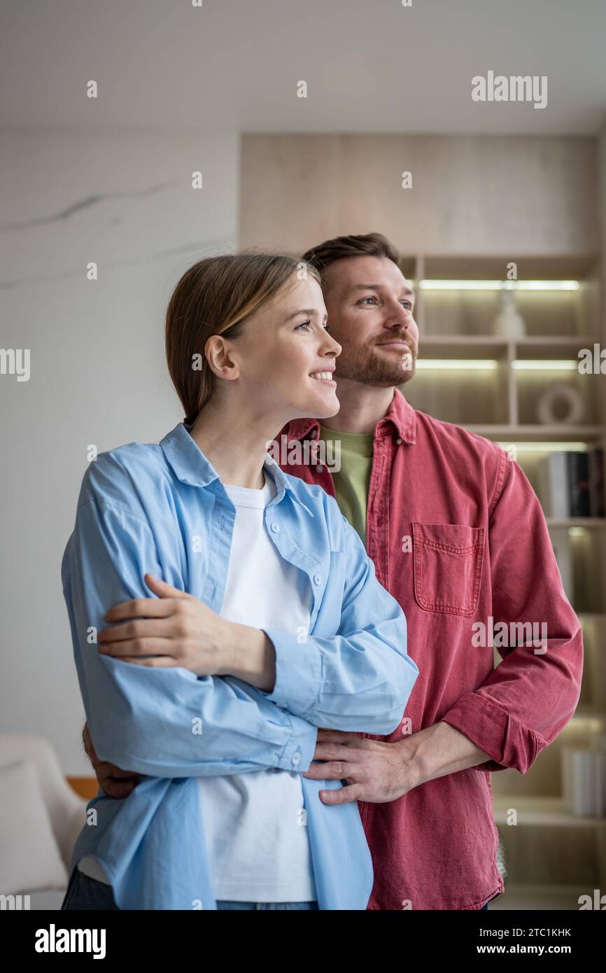 Gentle husband and tender wife standing embraced, looking at window ...