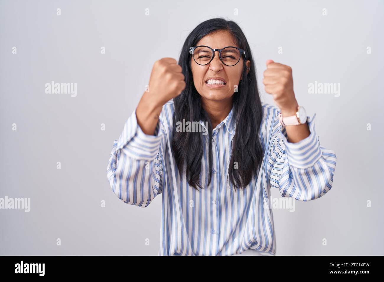 Young hispanic woman wearing glasses angry and mad raising fists ...