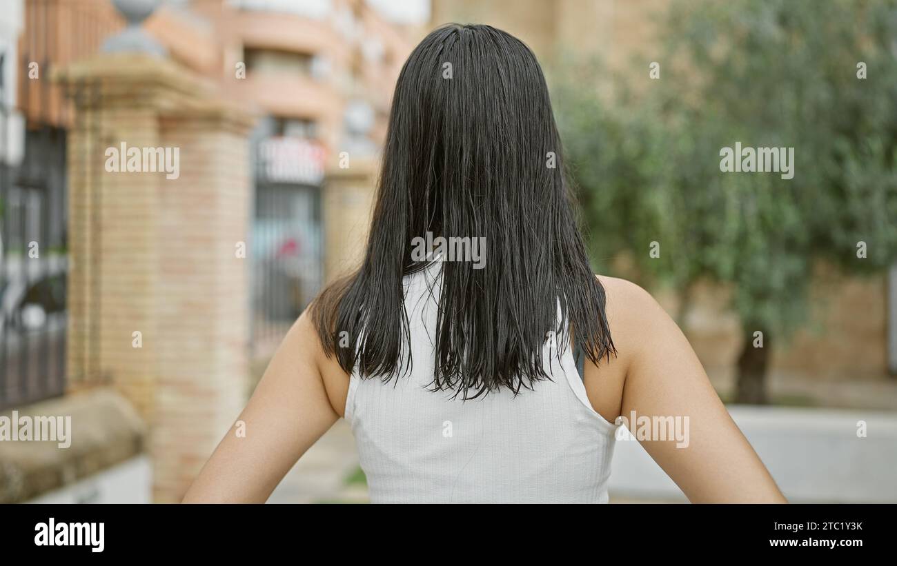 A young, beautiful hispanic woman caught in a casual, outdoor portrait, standing backward in a ...