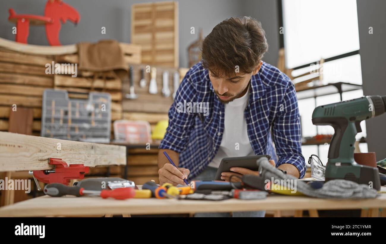 Diligent young arabian man jotting down ideas on touchpad in carpenter ...