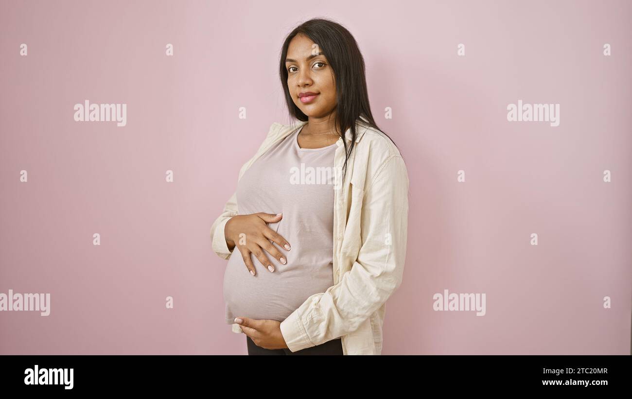 Expecting young woman touching her belly relaxed over isolated pink ...