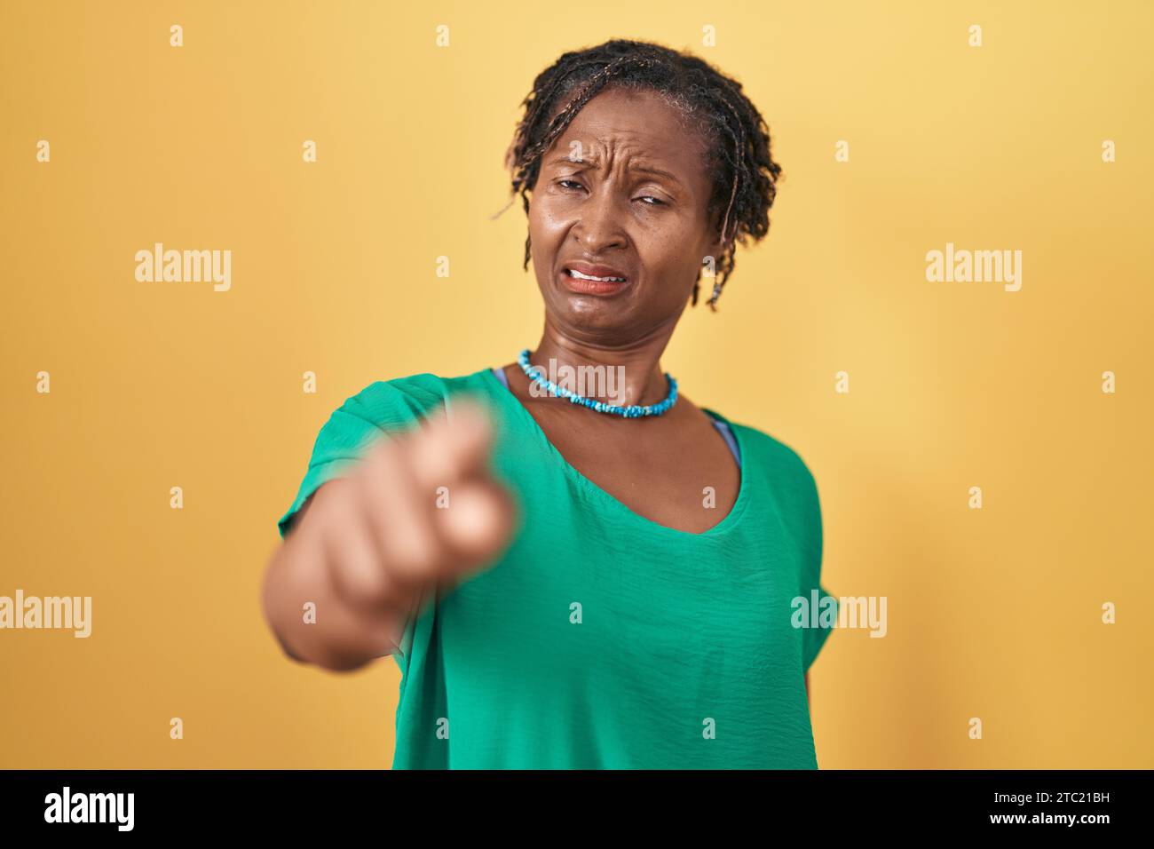 African woman with dreadlocks standing over yellow background pointing ...