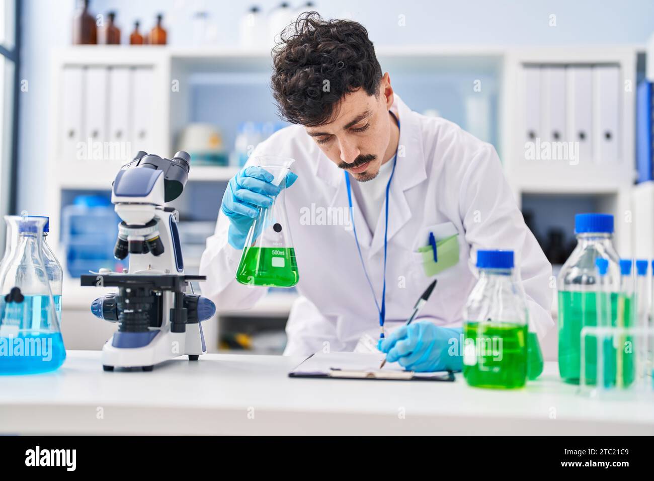 Young caucasian man scientist writing report holding test tube at ...