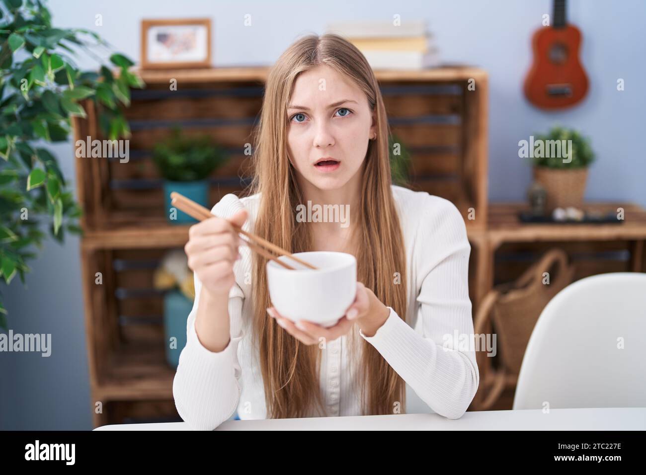 Young caucasian woman eating asian food using chopsticks in shock face ...