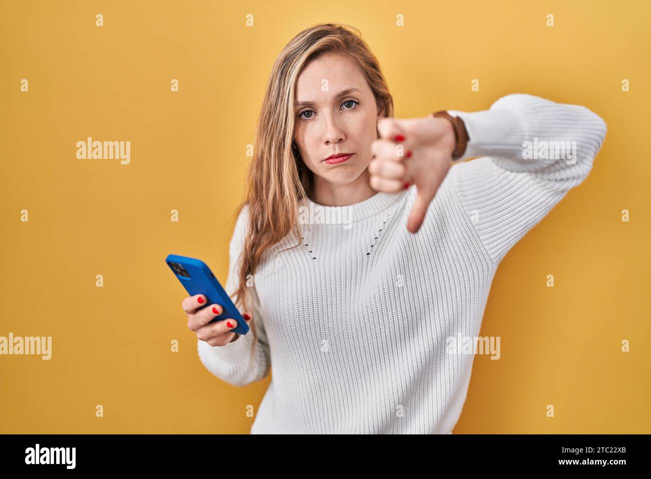Young blonde woman using smartphone typing message looking unhappy and ...