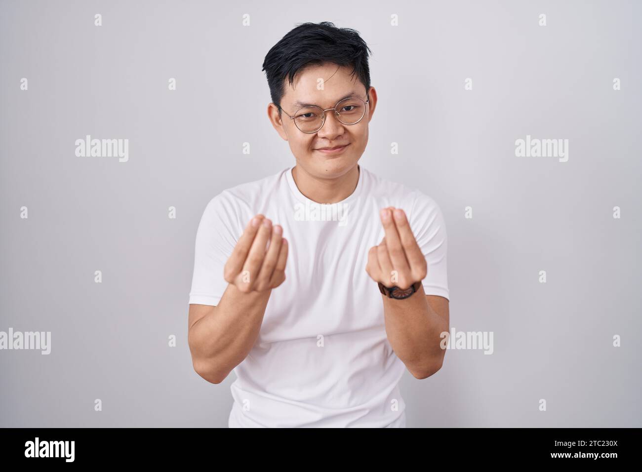 Young asian man standing over white background doing money gesture with ...