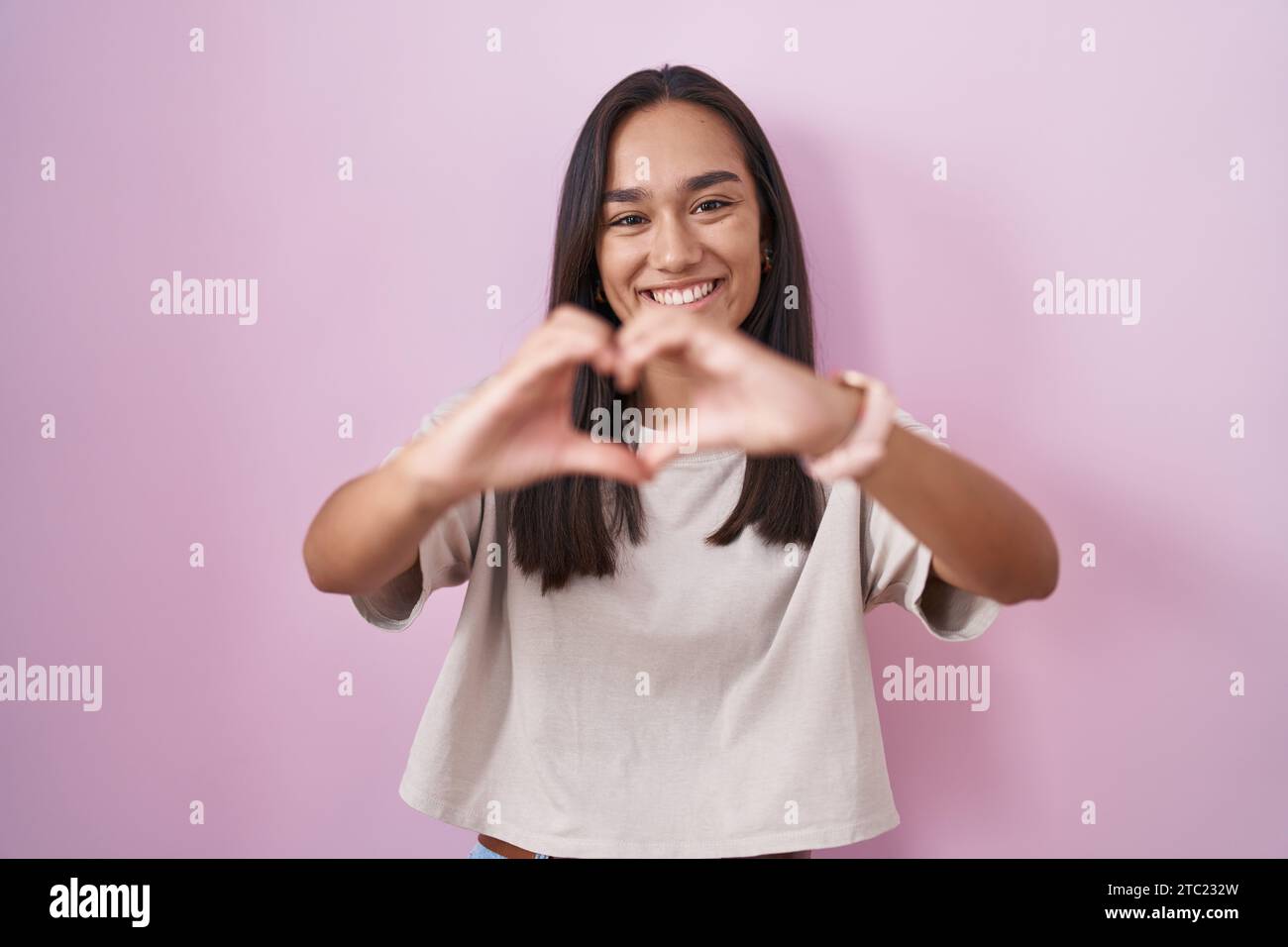 Young hispanic woman standing over pink background smiling in love ...