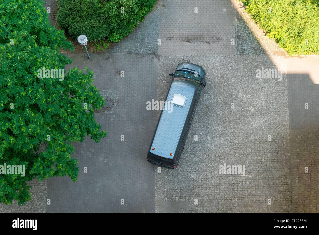 A photo from above on a long van on a paved area in the middle of trees ...