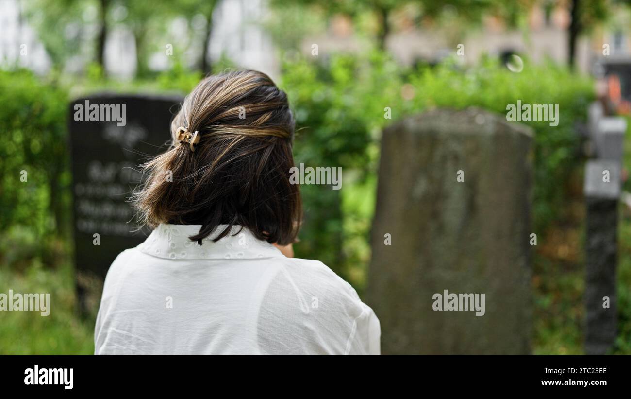 Beautiful young hispanic woman praying and mourning by tombstone at ...