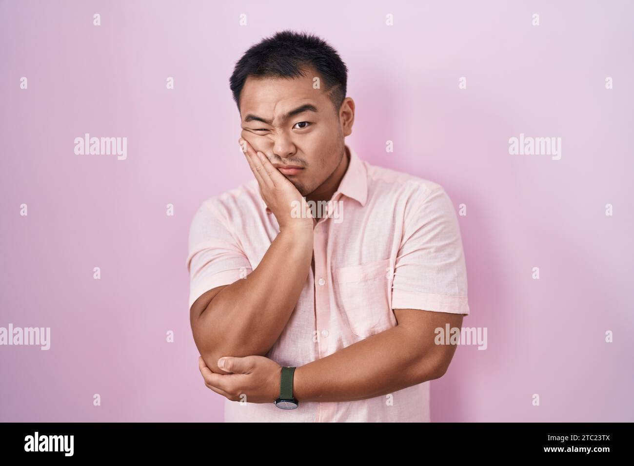 Chinese young man standing over pink background thinking looking tired ...
