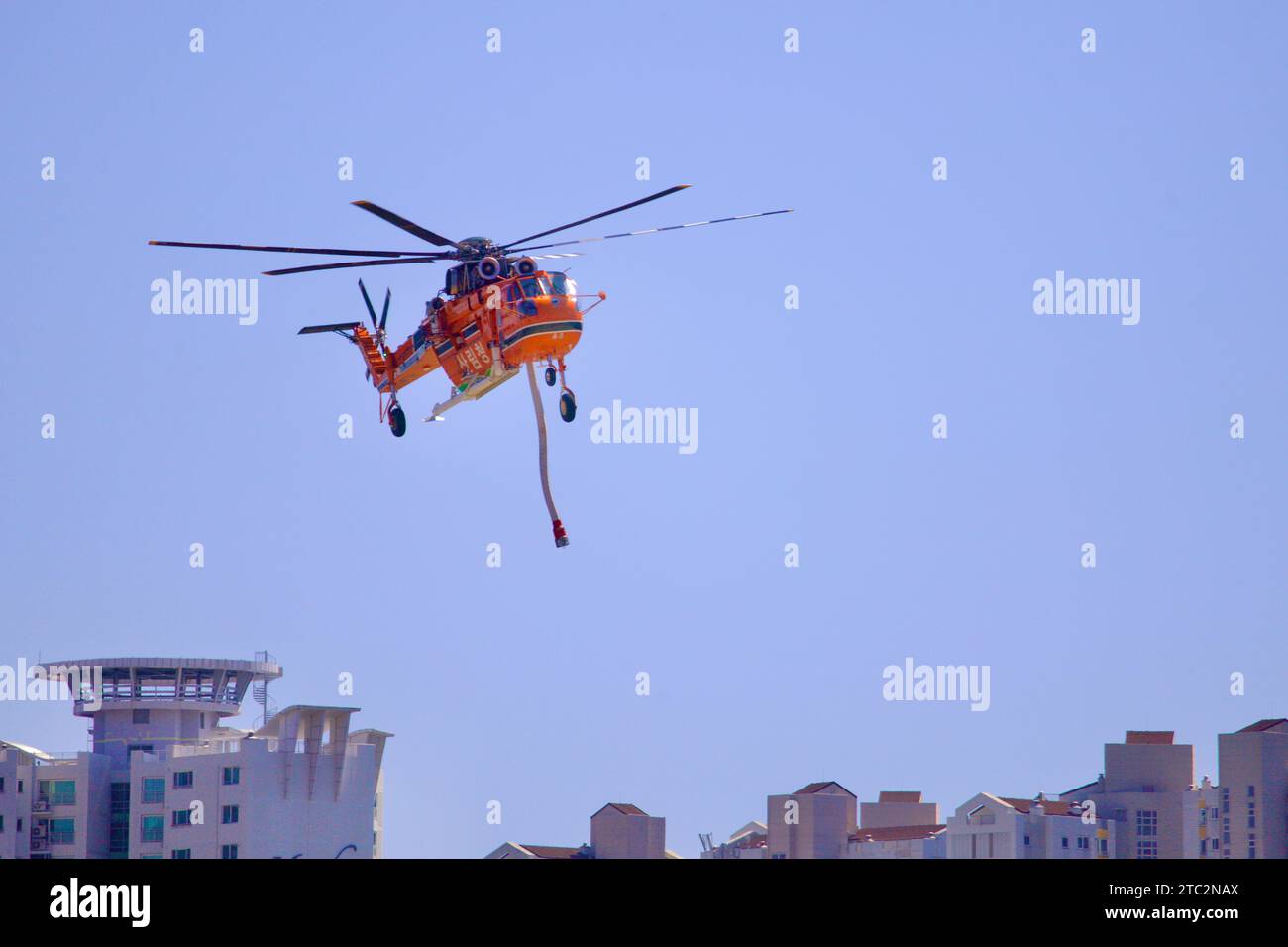 A firefighting helicopter descends for landing, framed by towering ...