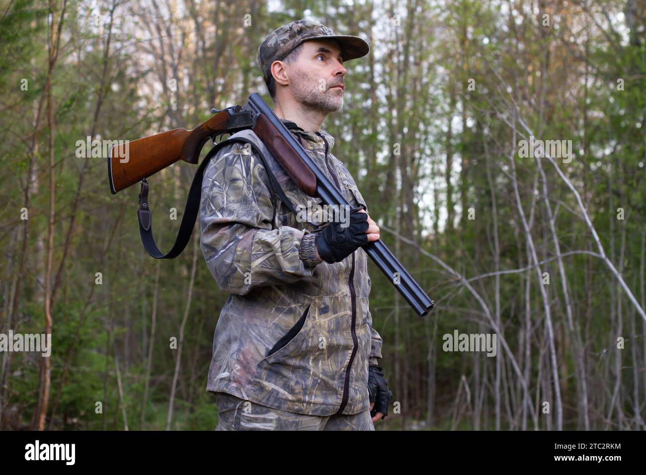 A hunter holds an unloaded rifle on his shoulder in the evening in a ...