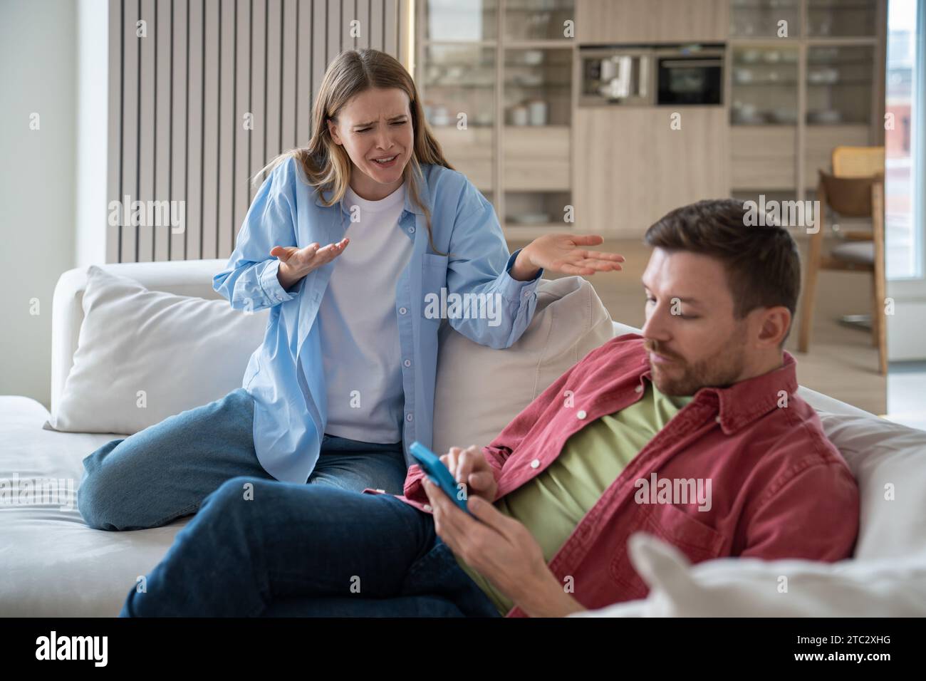 Nervous reproachful wife shouting at calm neglecting husband sitting on ...