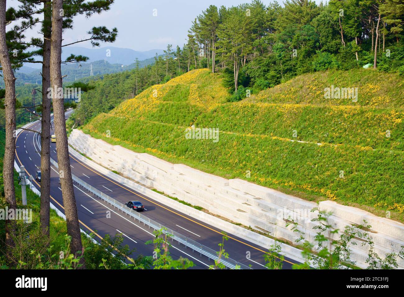 A four-laned highway carves through a shallow valley in Korea, flanked ...