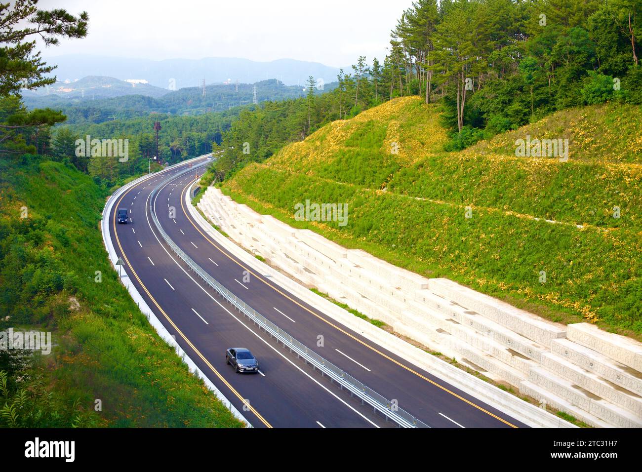A four-laned highway carves through a shallow valley in Korea, flanked ...