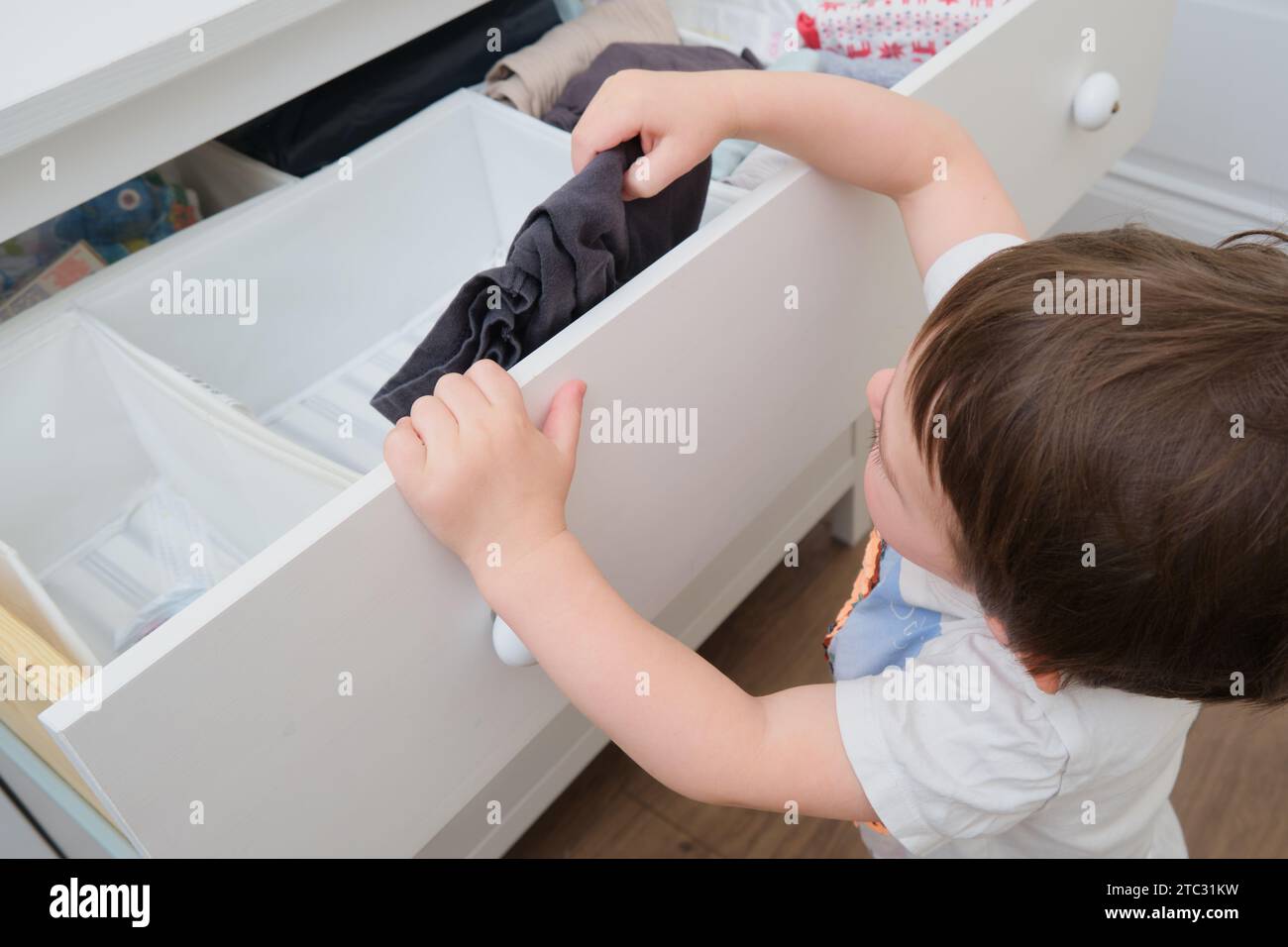 Cute little baby boy putting clothes in chest of drawers at home. Kid ...
