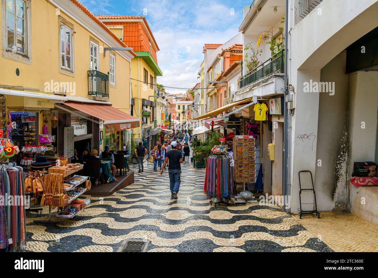 A busy street of shops and sidewalk cafes with traditional Calcada ...