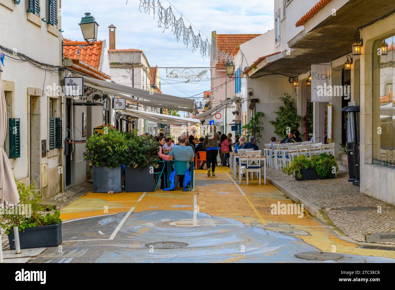 A busy street of shops and sidewalk cafes with traditional Calcada ...