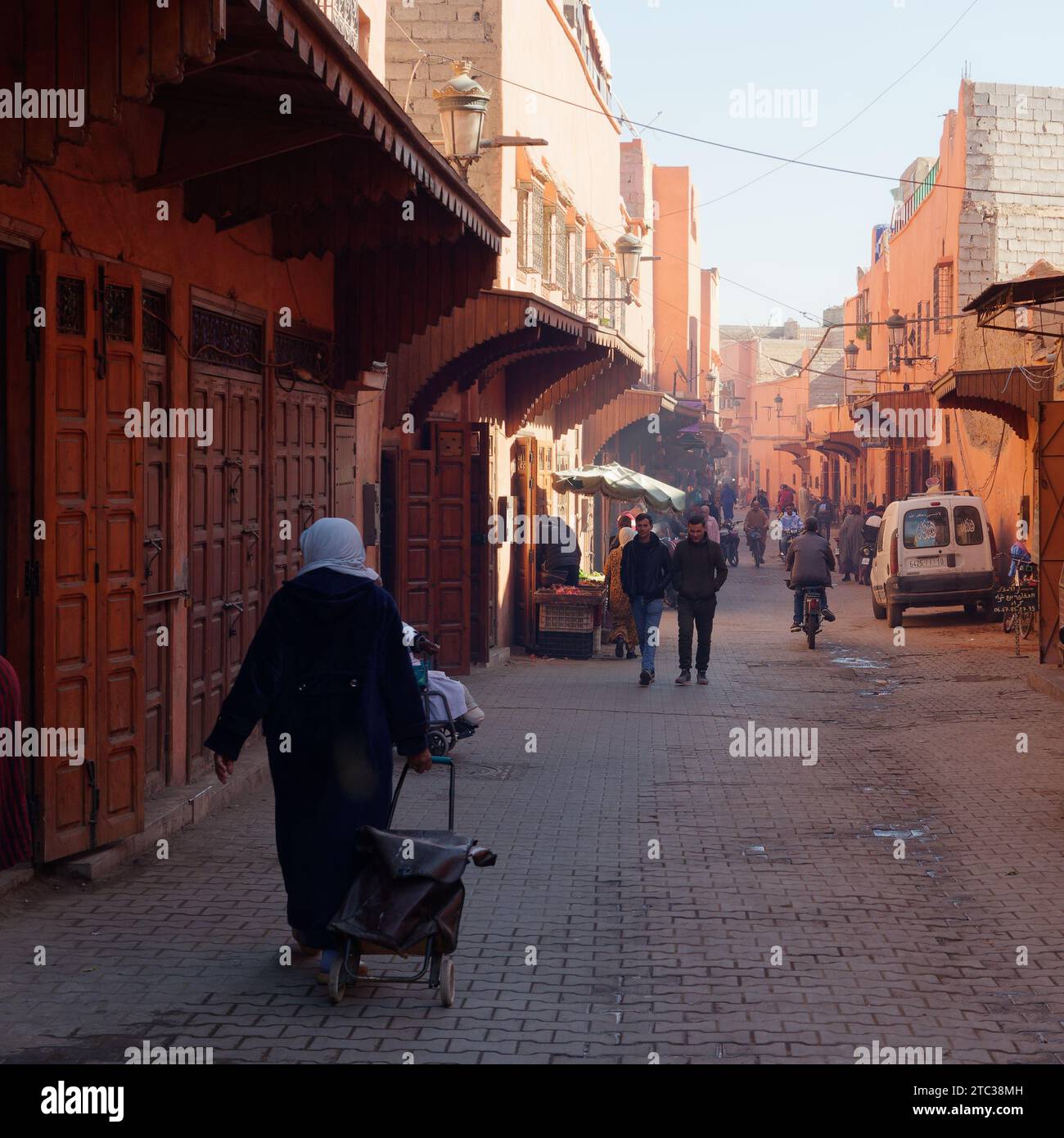 Lady walks down a street with shopping trolley in the city of Marrakesh ...