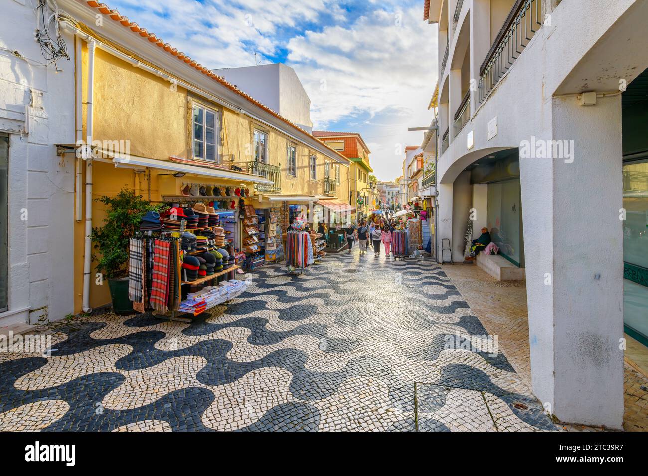 A busy street of shops and sidewalk cafes with traditional Calcada ...