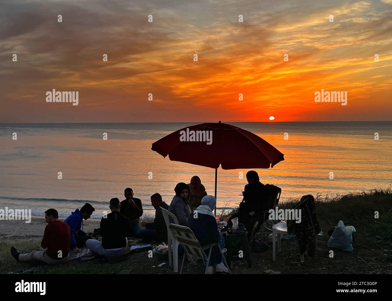 People enjoy the warm weather as the sun sets at a waterfront promenade ...