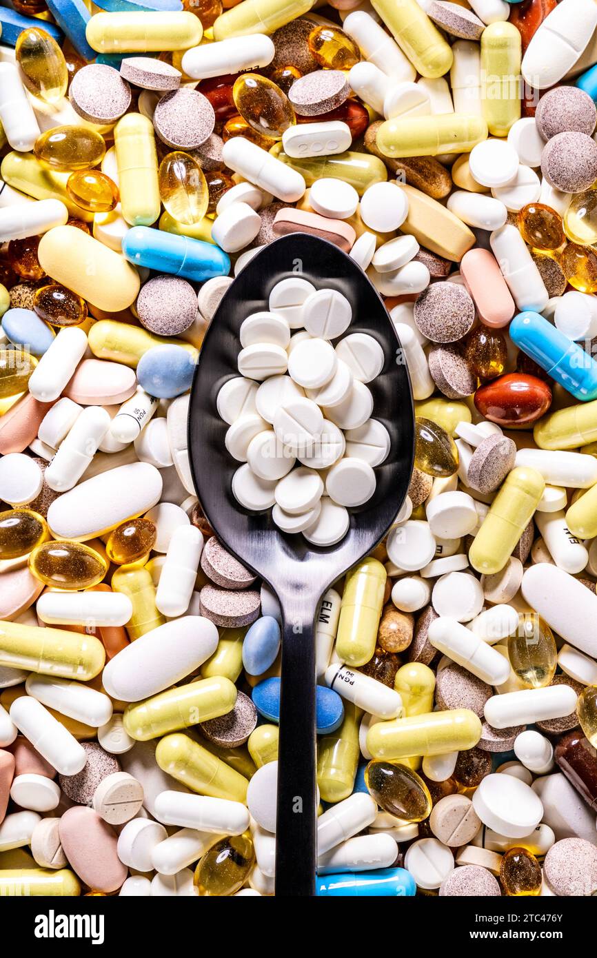 Round pills on a spoon with pills, tablets and capsules in background ...