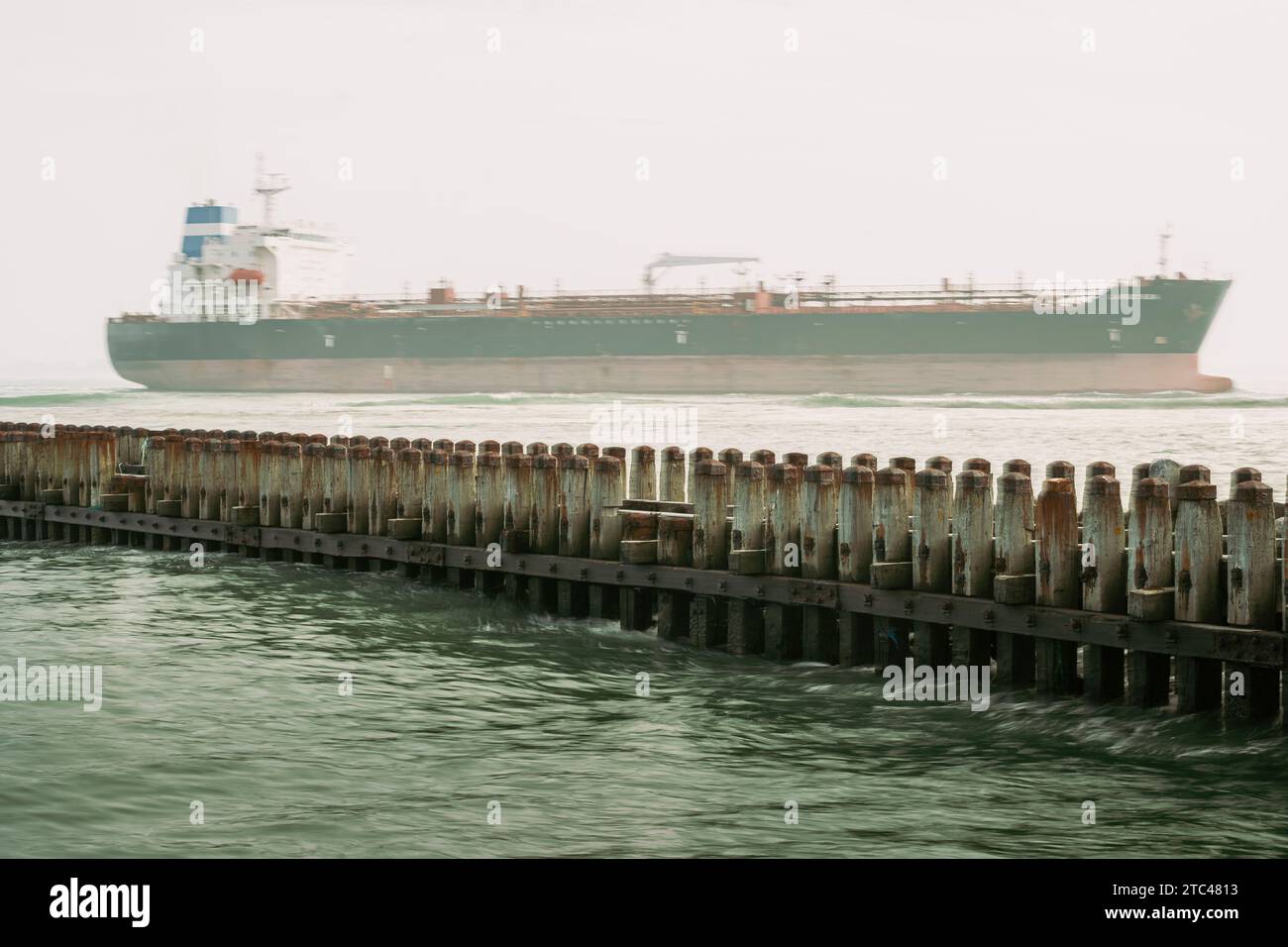 Large tanker ship sailing at sea with motion blur passing breakwater at ...