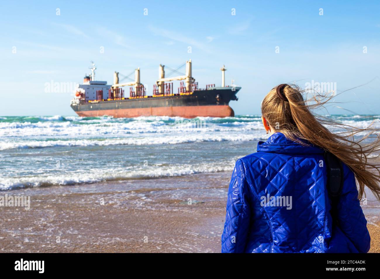 A woman at sea looks at a stranded cargo ship that was thrown out ...