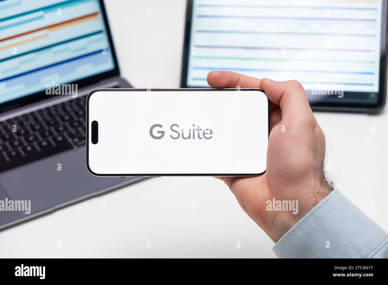 G Suite logo on the screen of a smartphone in mans hand with laptop and ...