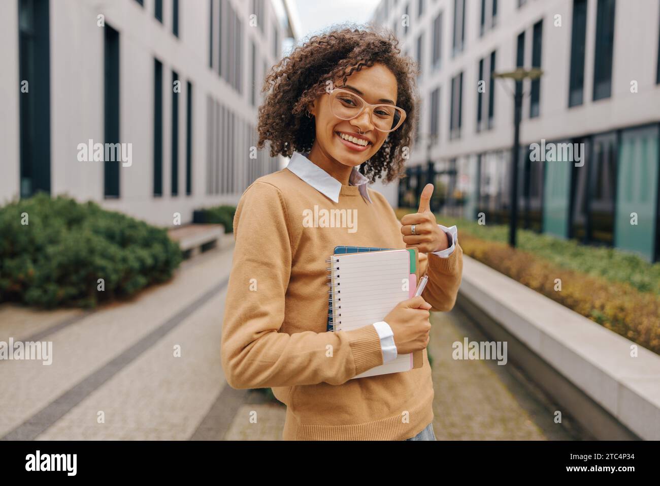 Young female student standing with note pads on modern building ...