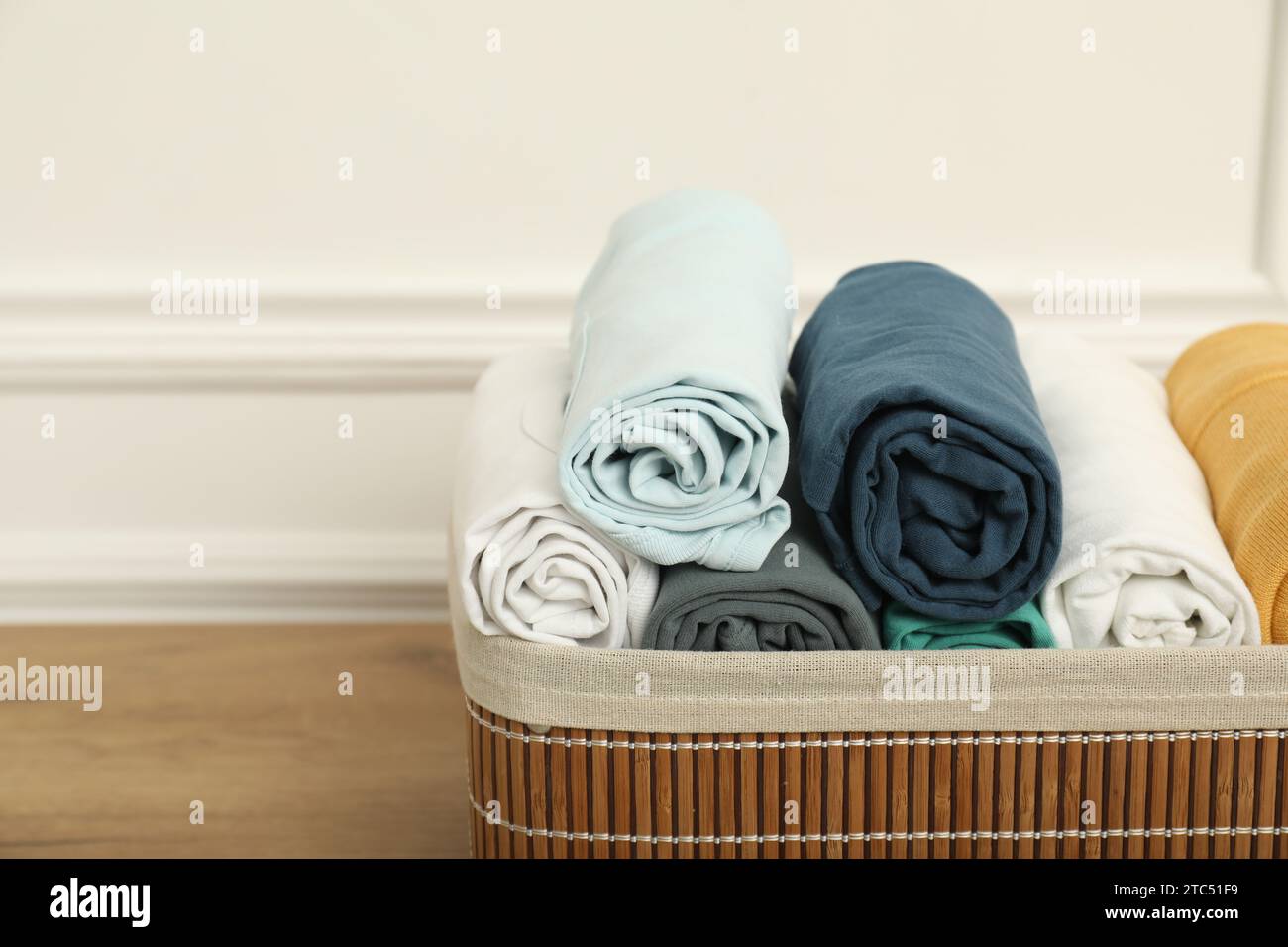 Basket with different rolled clothes on wooden table near white wall ...