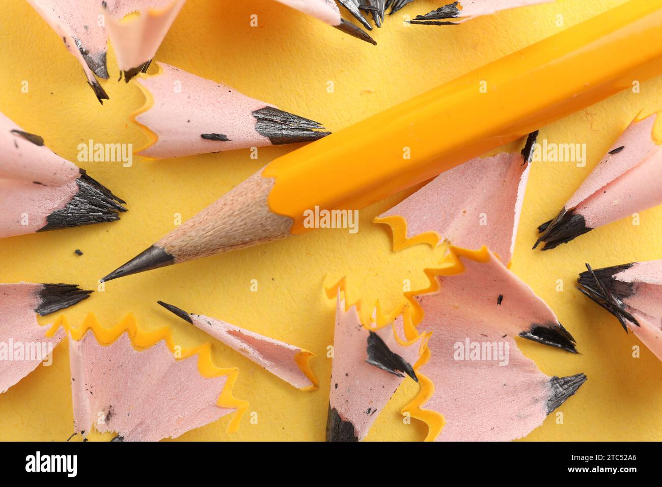 One sharp graphite pencil and shavings on yellow background, top view ...