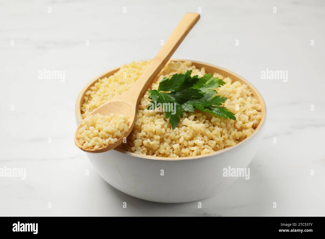 Delicious bulgur with parsley and spoon on white marble table, closeup ...
