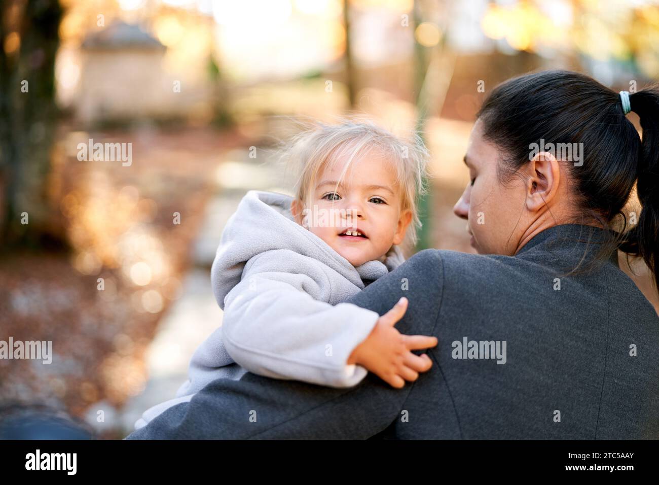 Smiling little girl peeking over her mother shoulder while sitting in ...