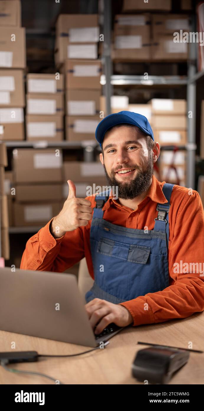 Warehouse worker smiling and thumbs up while working with inventory in ...
