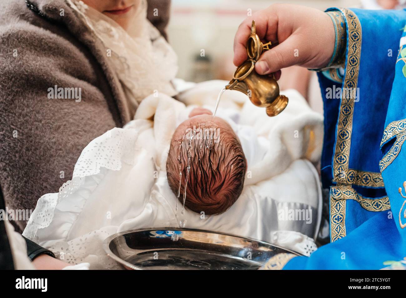 A priest pours water on the head of a small child during the Christian ...